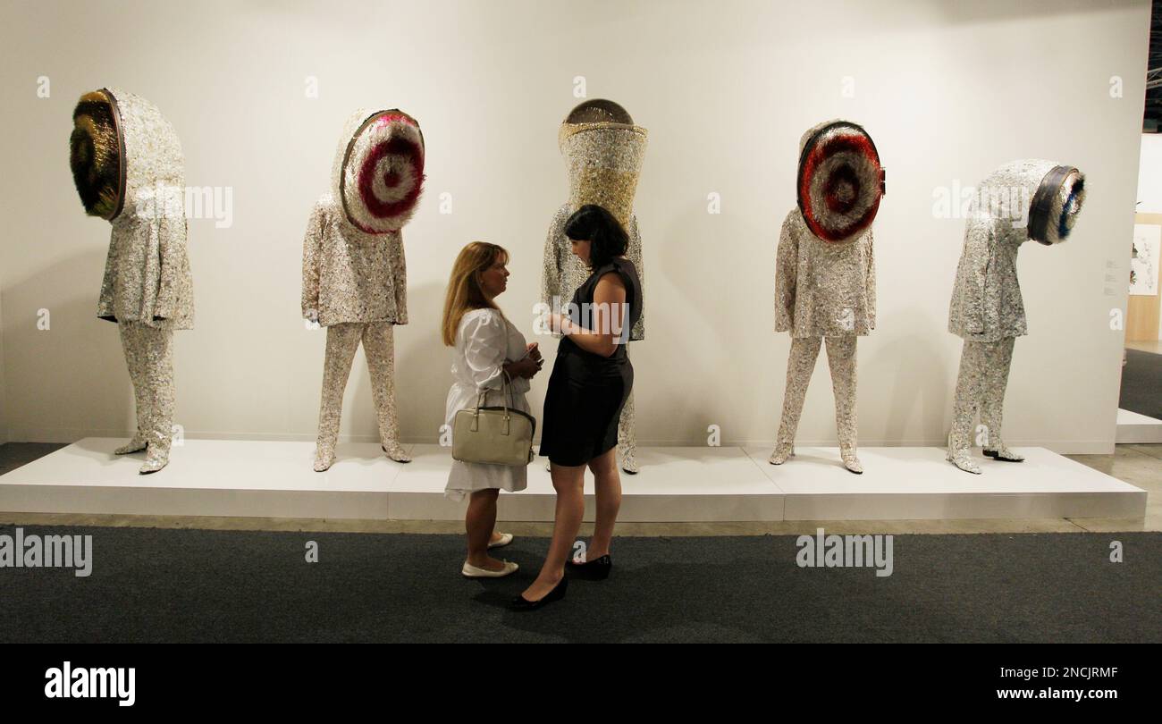 Two women talk as they stand in front of Nick Cave's Soundsuit 2010 art ...