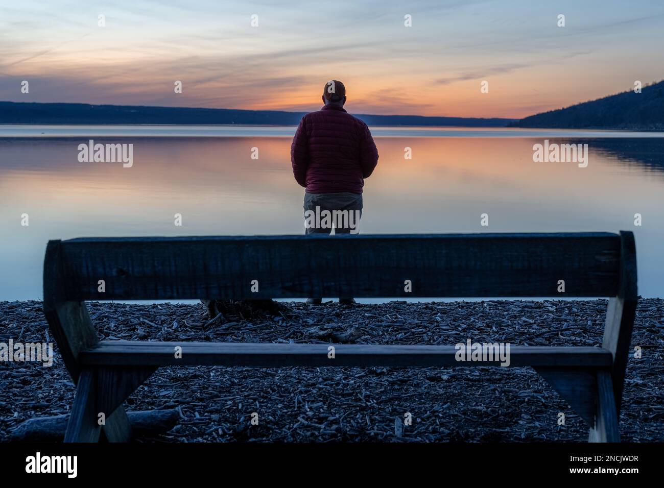 Winter scene of a man with red jacket along a beach looking out over a ...