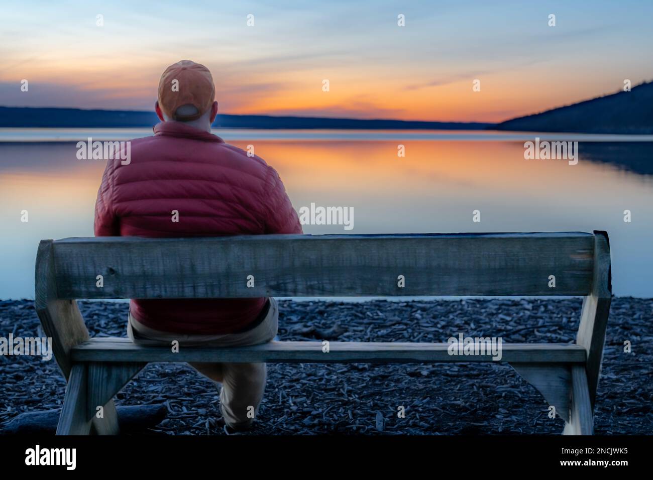 Winter scene of a man with red jacket on a bench looking out over a ...