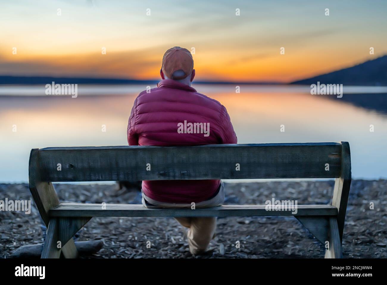 Winter scene of a man with red jacket on a bench looking out over a ...