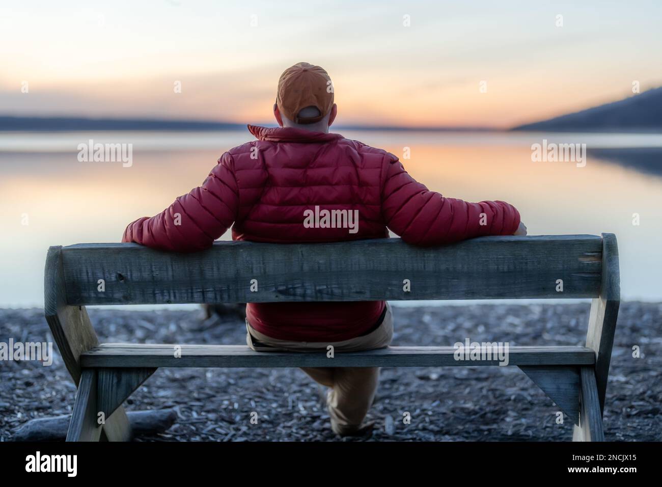 Winter scene of a man with red jacket on a bench looking out over a ...