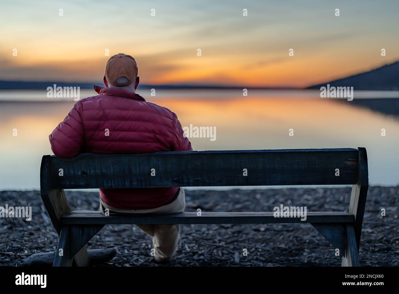 Winter scene of a man with red jacket on a bench looking out over a ...
