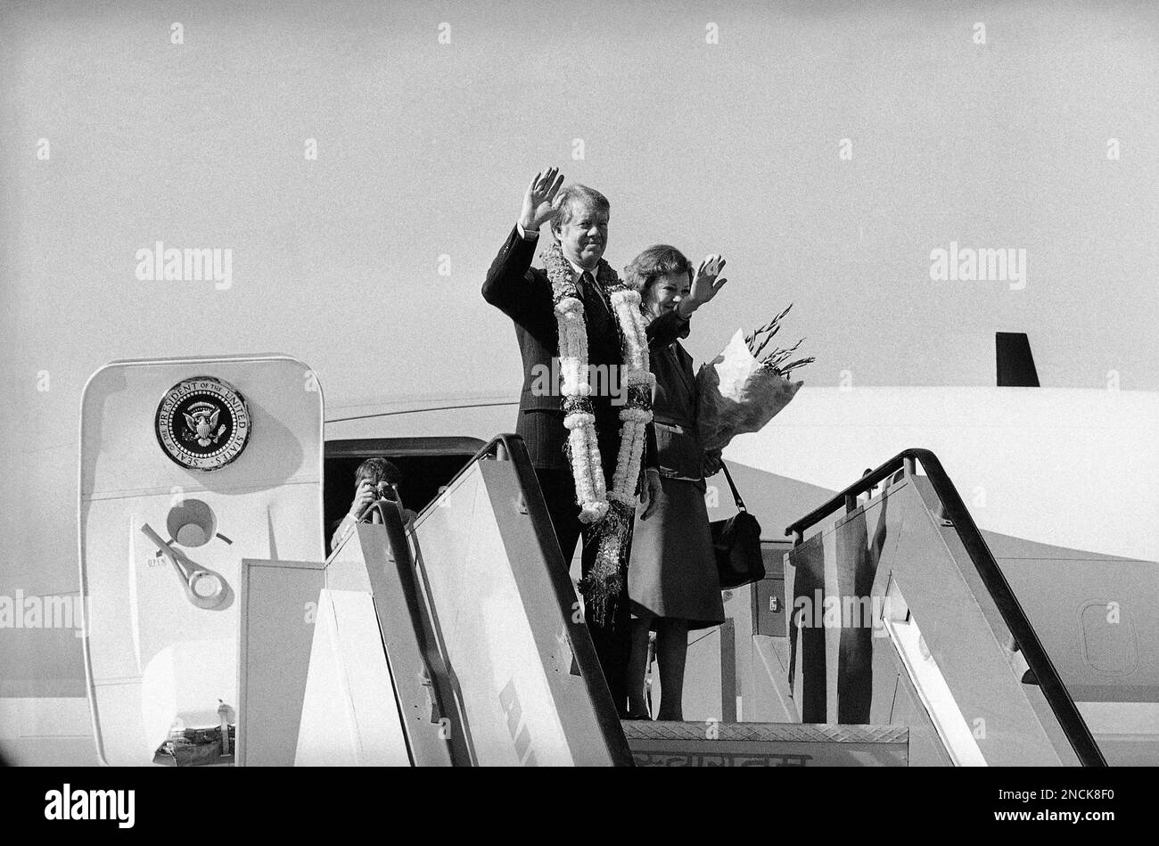 A garlanded President Jimmy Carter and first lady Rosalynn Carter wave ...