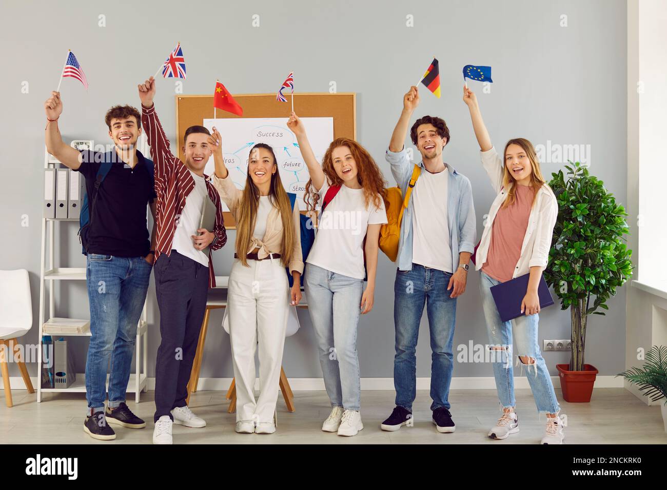 Happy international students standing in classroom, holding up flags ...