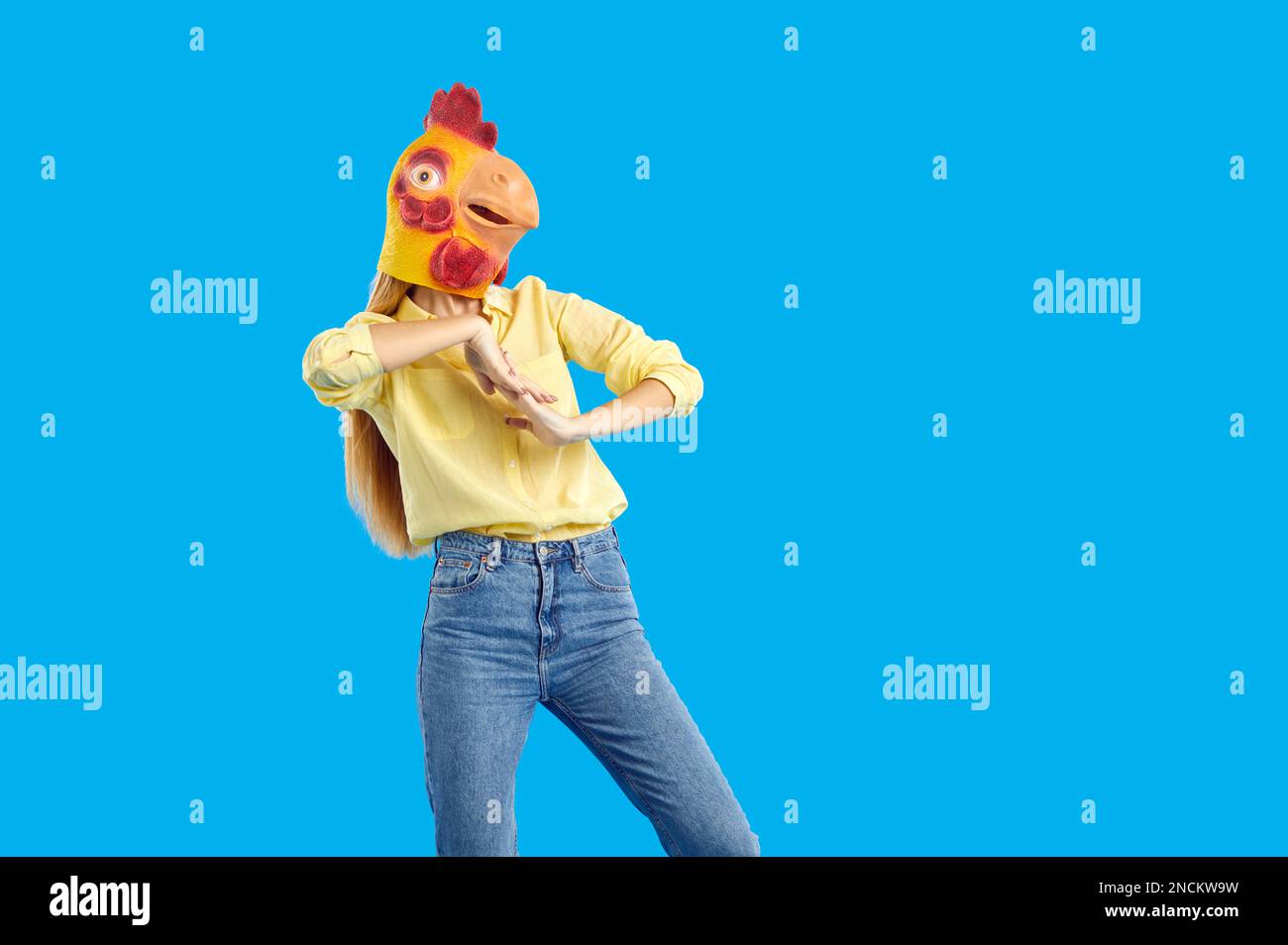 Young woman wearing funny strange chicken mask dancing on blue studio ...