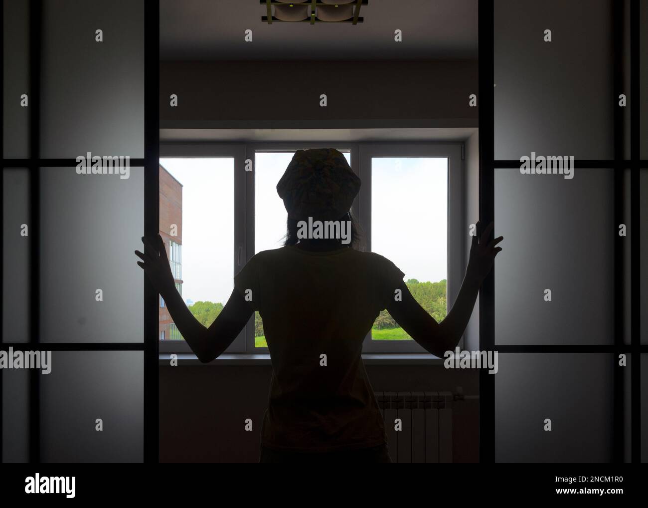 Girl in a t-shirt and hat, standing in the shadows of the room, pushing ...