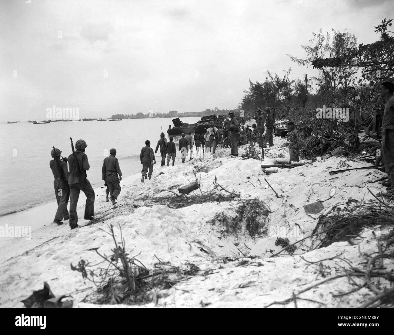 Japanese prisoners of war walk in single file along the beach headed ...