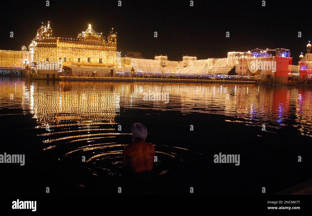 An Indian Sikh devotee bathes in holy water in front of the illuminated ...
