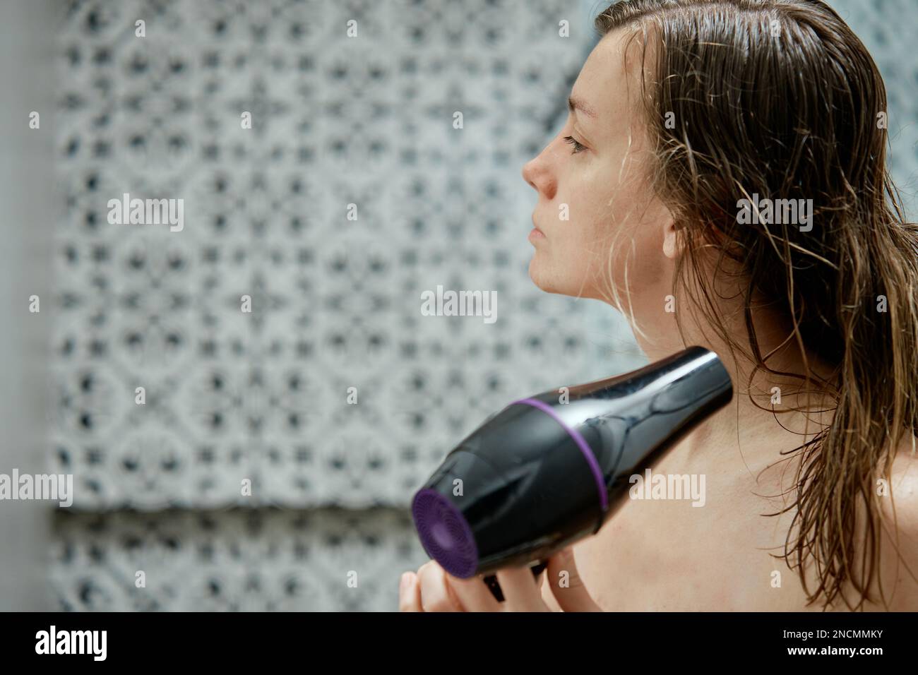 Woman wrapped in towel blow drying hairs standing in bathroom. Female ...