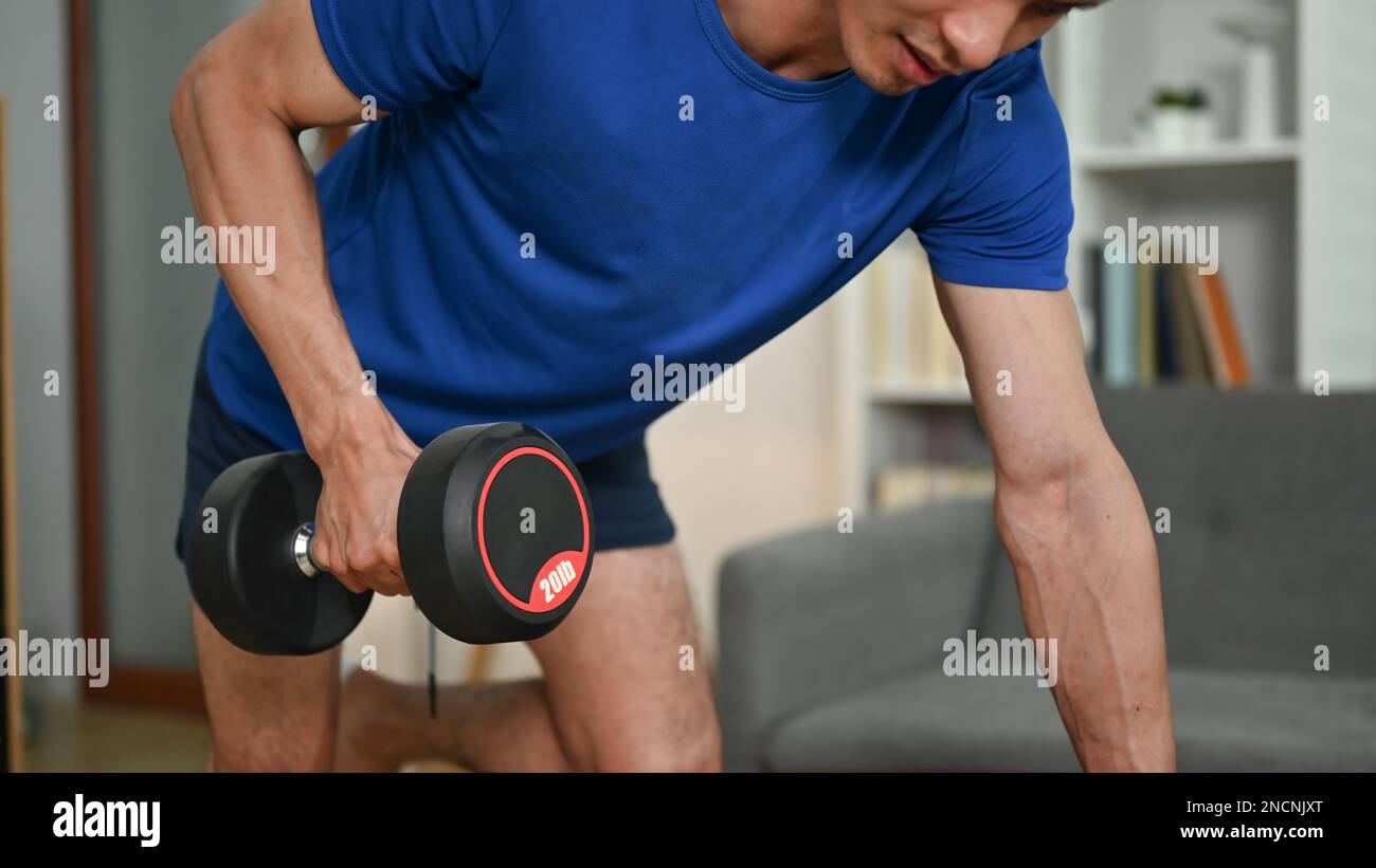 Muscular asian man bodybuilder exercising with heavy dumbbell at home ...