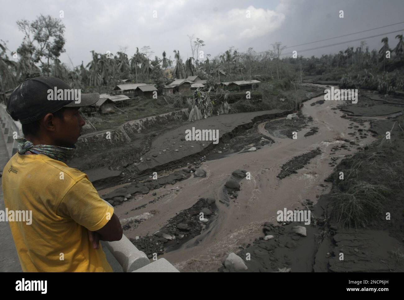 A man stands on a bridge overlooking a river carrying volcanic ash from ...