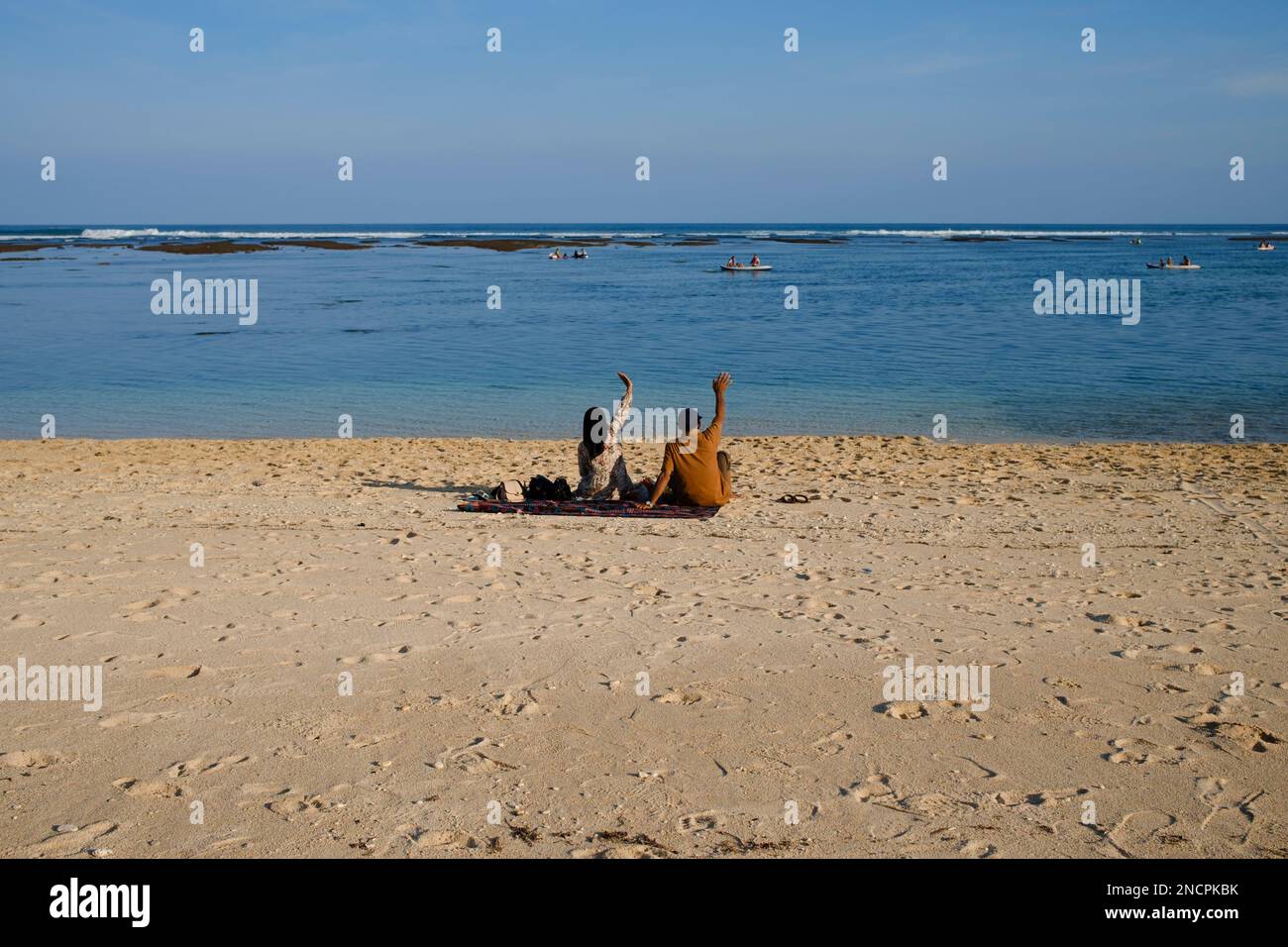 Parents sitting on the beach and waing their hands to their kids at ...