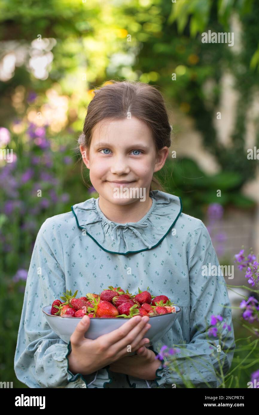 Cute little girl in a vintage dress with a bowl of ripe strawberries in ...