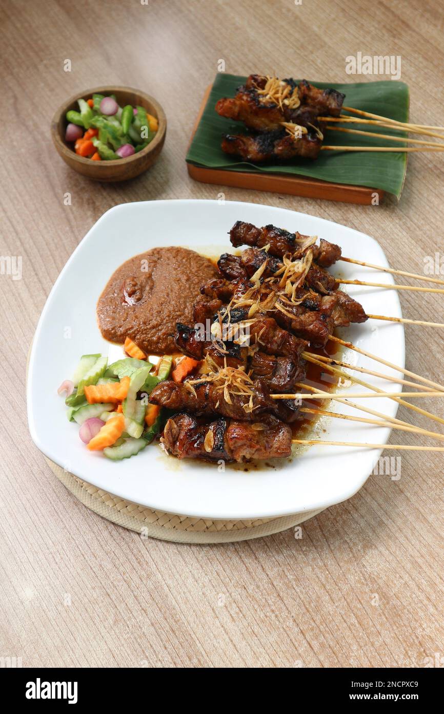 serving of beef satay with pickled cucumber slices, peanut sauce and a ...