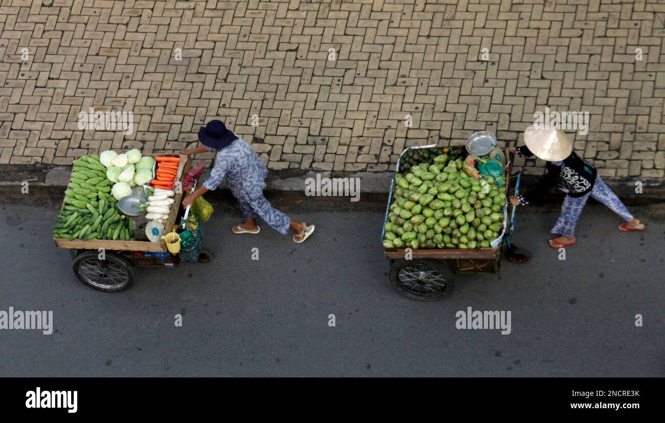 Vietnamese street vendors push carts of fruits and vegetables, in Ho ...