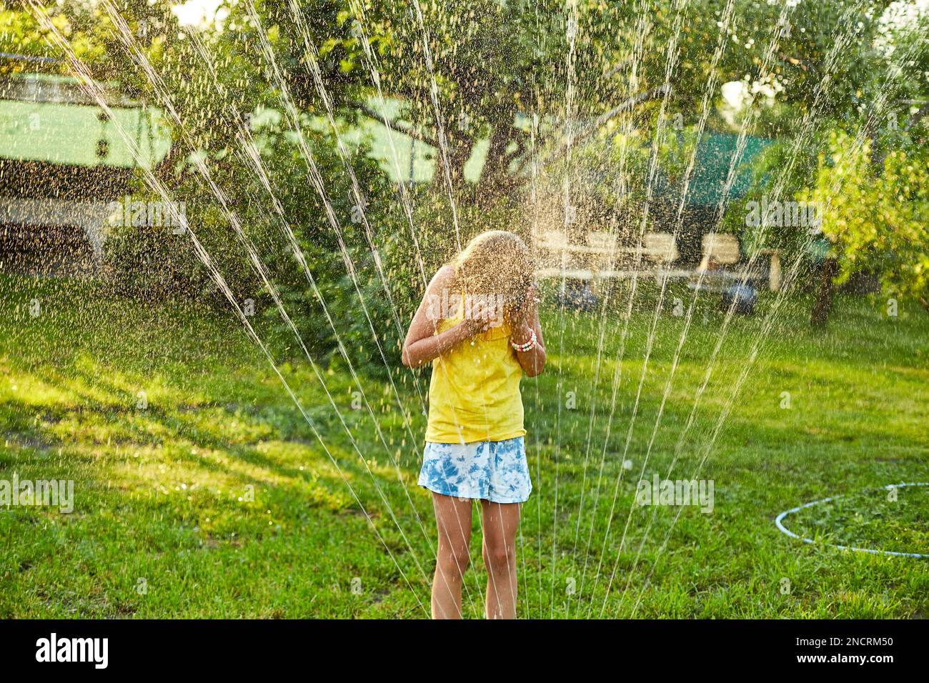 Happy kid girl playing with garden sprinkler run and jump, summer ...