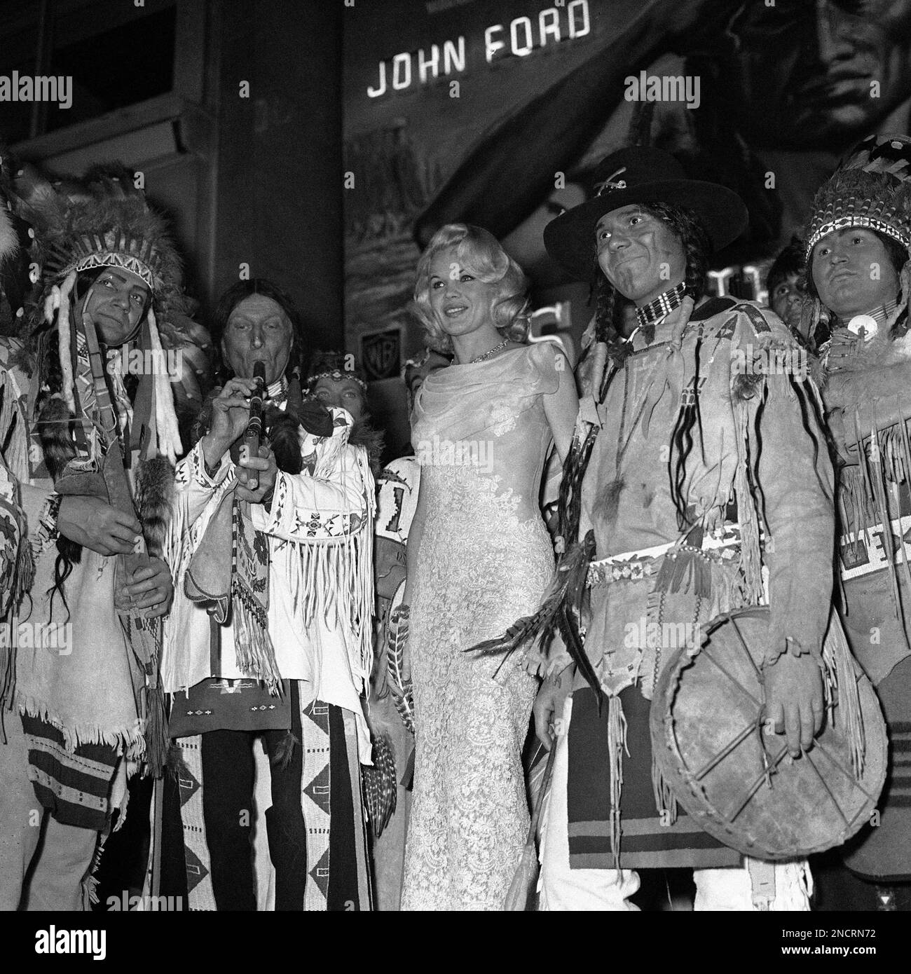 American actress Carroll Baker poses with some men dressed up as Native ...