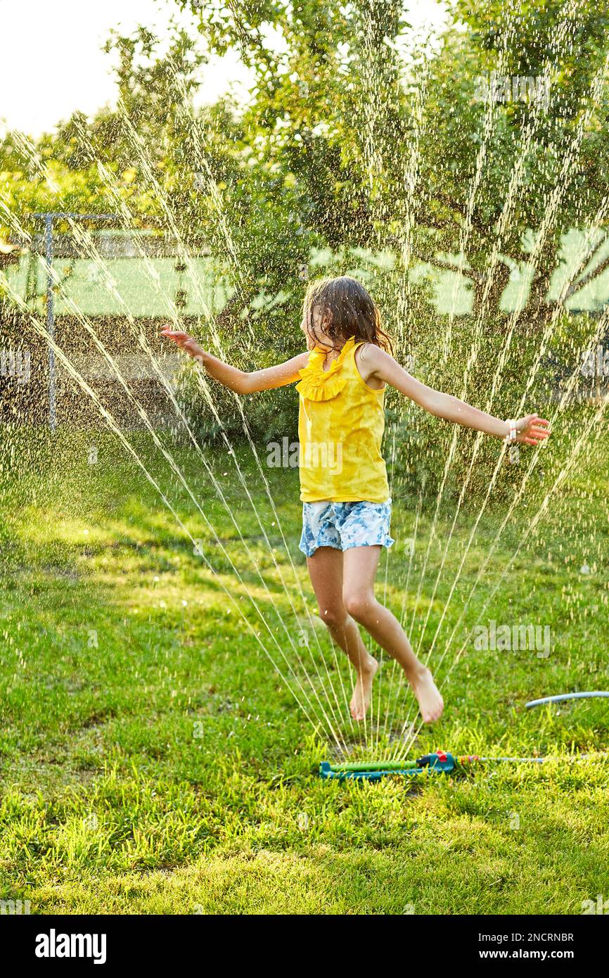 Happy kid girl playing with garden sprinkler run and jump, summer ...