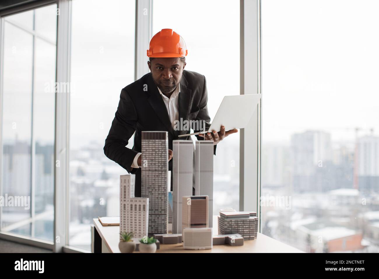 Focused african inspector using laptop inspecting skyscraper model in ...