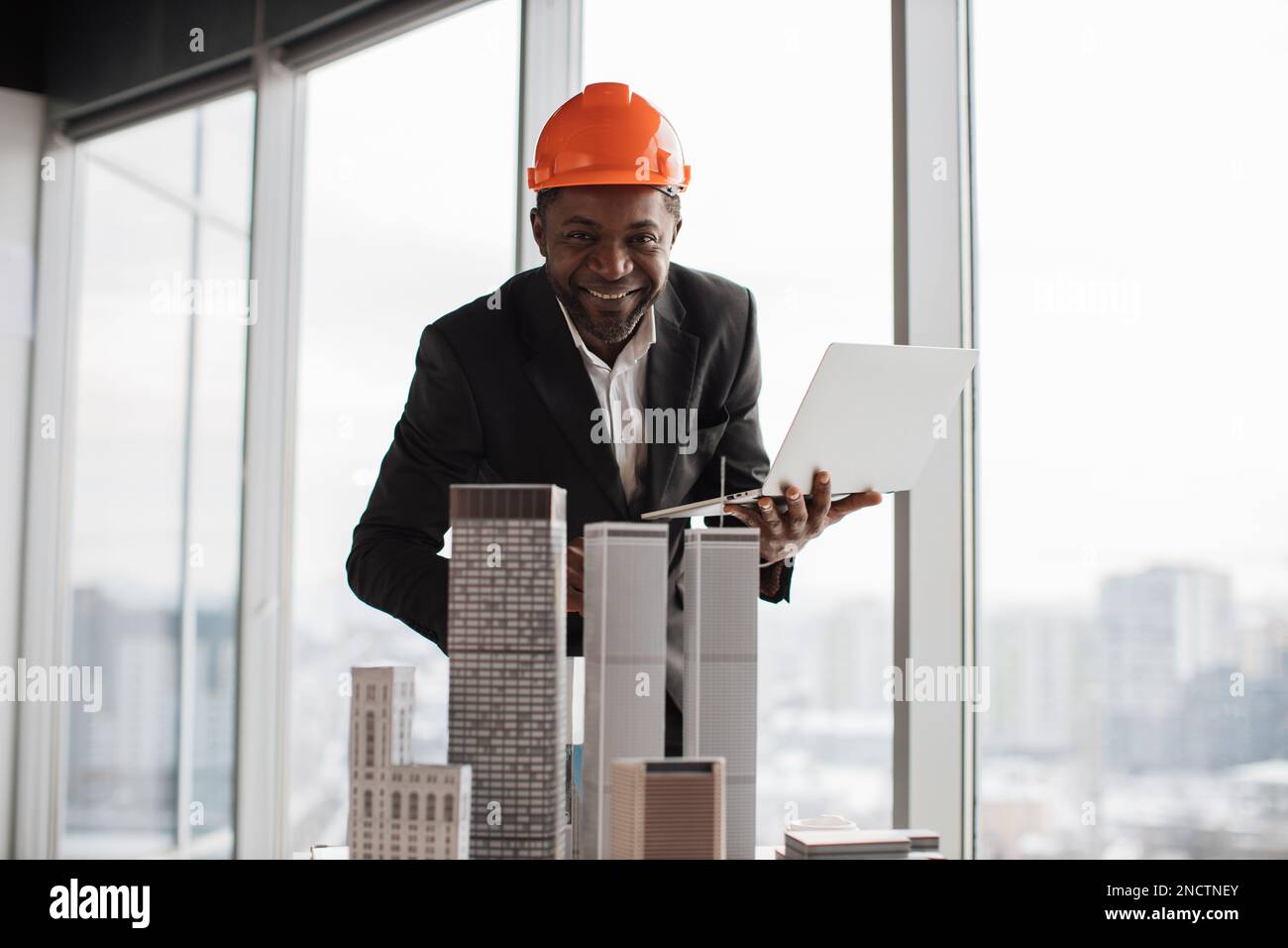Focused african inspector using laptop inspecting skyscraper model in ...