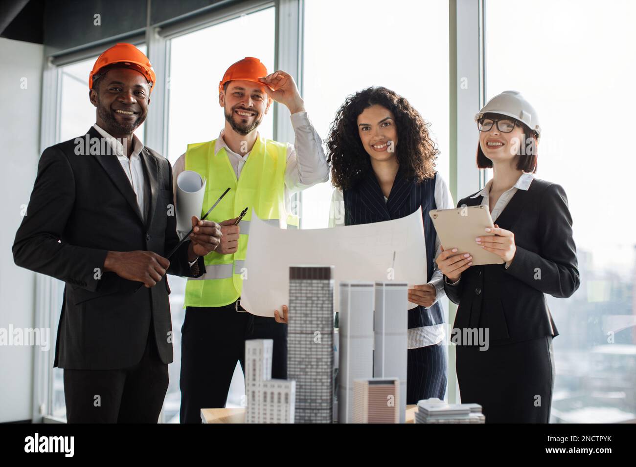 Group of four colleagues standing near building complex prototype ...