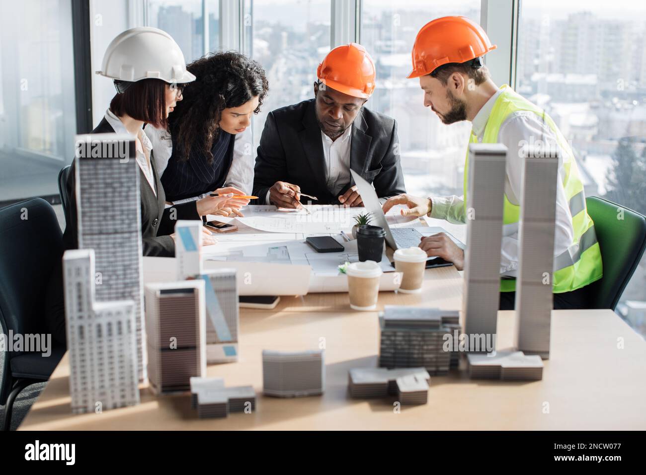Group of four multiracial people architects sitting at desk with lots ...