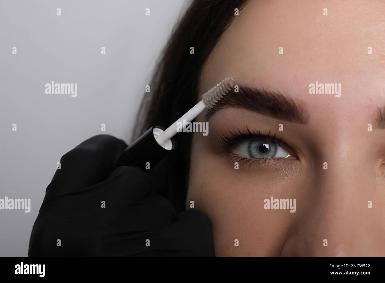 Beautician fixing woman's eyebrows with gel after tinting on light grey ...