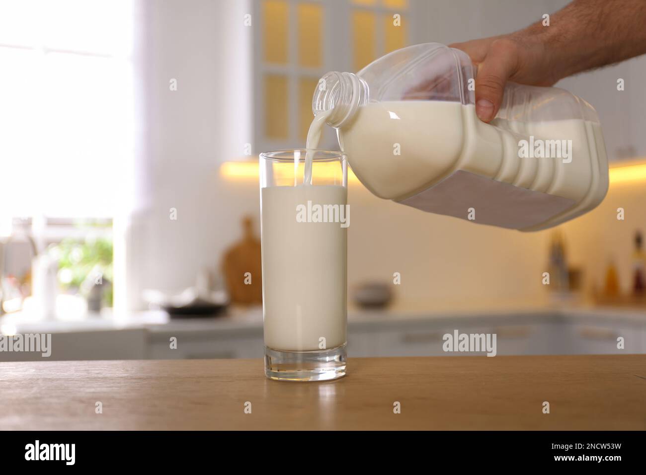 Man pouring milk from gallon bottle into glass at wooden table in ...