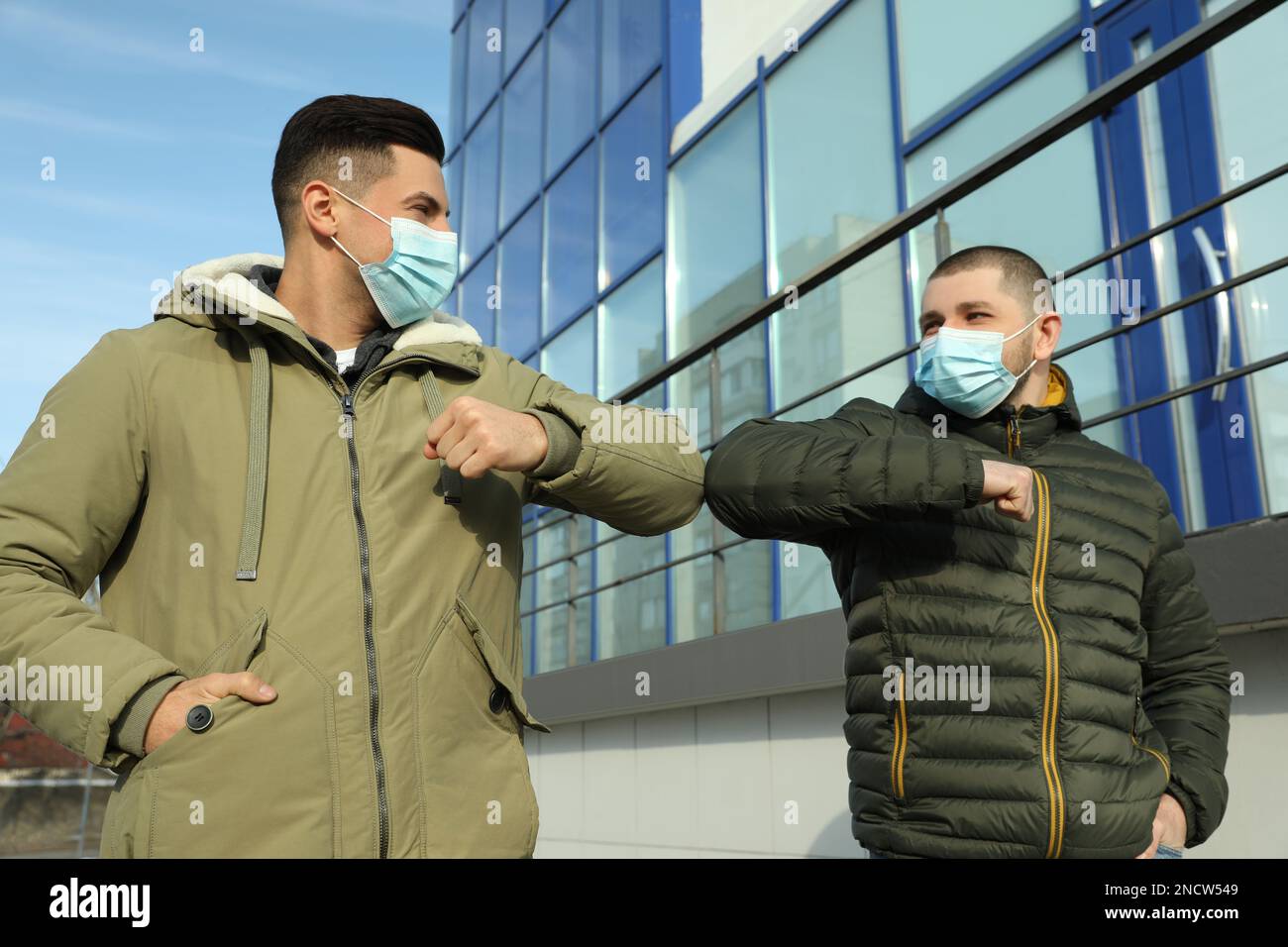 Men in masks greeting each other by bumping elbows outdoors Stock Photo ...