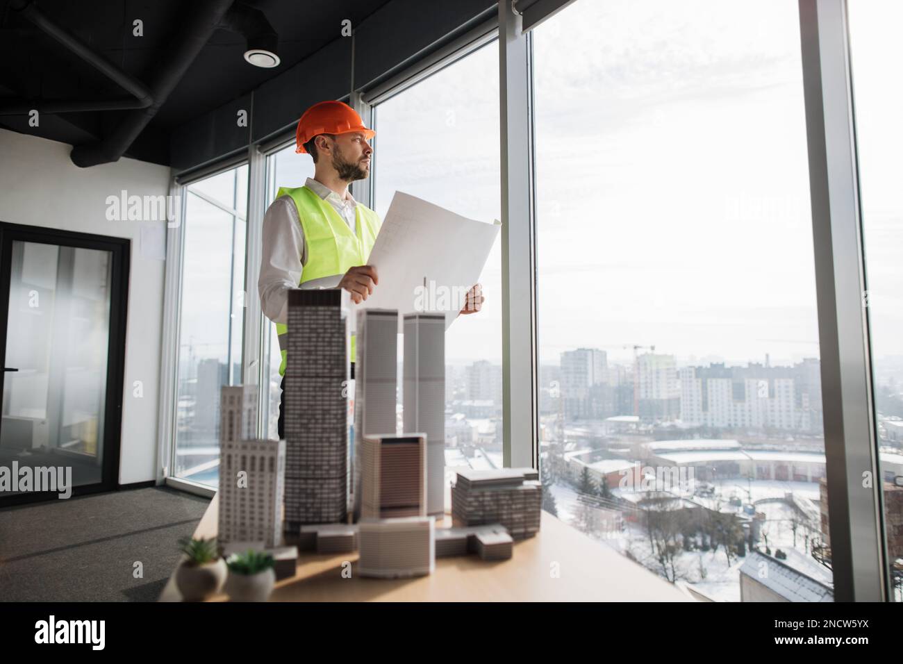 Engineer man in helmet and reflective vest holding blueprint standing ...