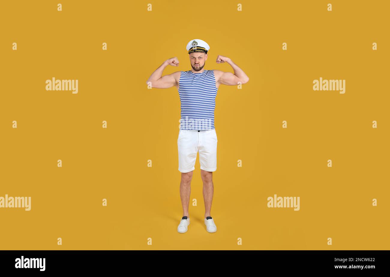 Strong sailor showing biceps on yellow background Stock Photo - Alamy