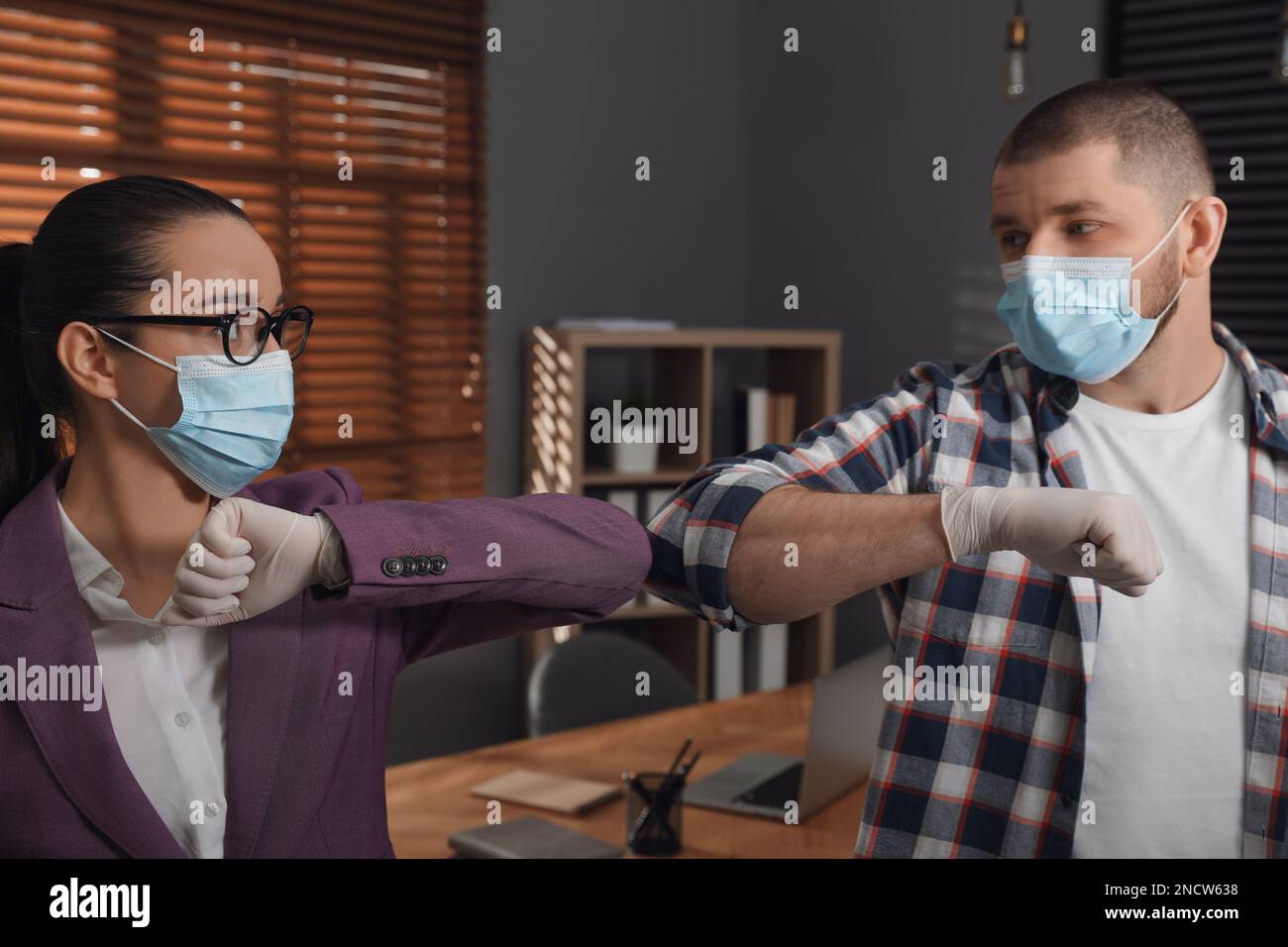 Office employees in masks greeting each other by bumping elbows at ...