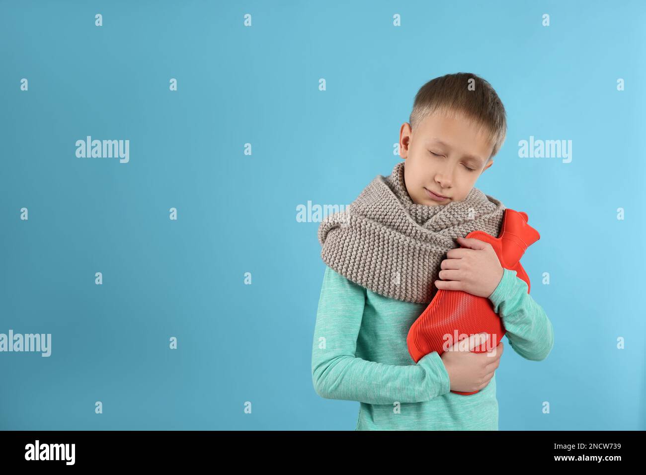 Ill boy with hot water bottle suffering from cold on light blue ...
