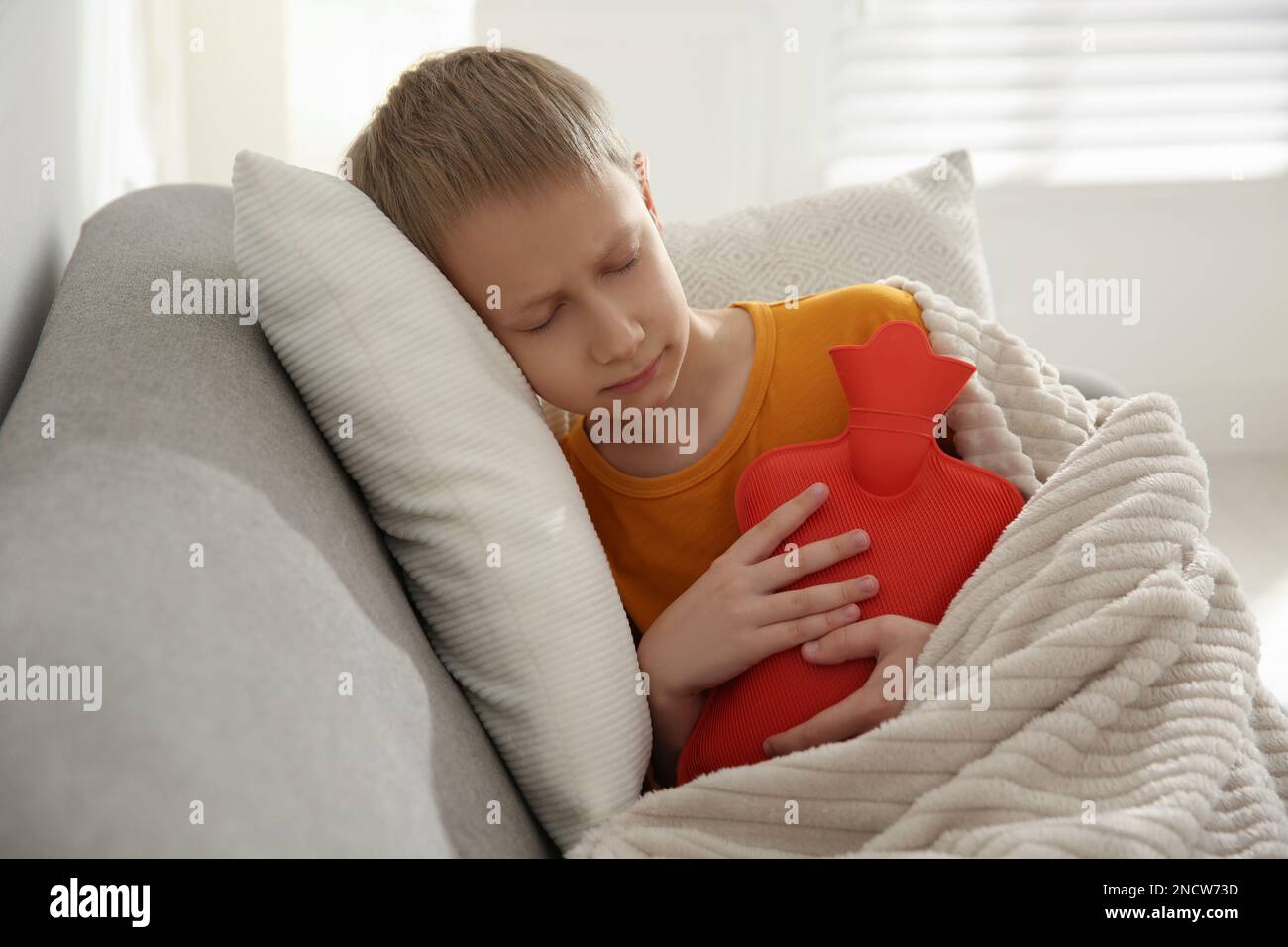 Ill boy with hot water bottle suffering from cold at home Stock Photo ...