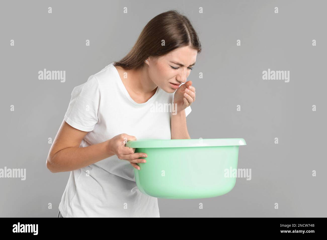 Woman with basin suffering from nausea on grey background. Food ...
