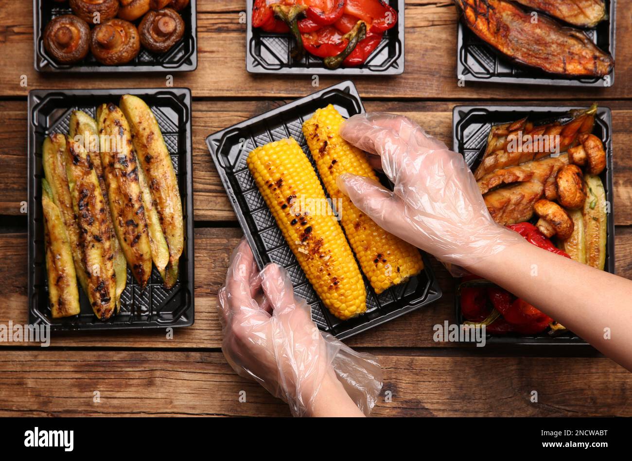 Waiter in gloves putting grilled corn cobs into containers at wooden ...
