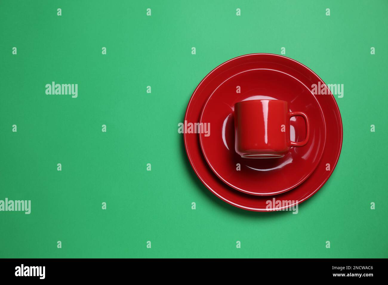Set of red ceramic dishware on green background, top view. Space for ...