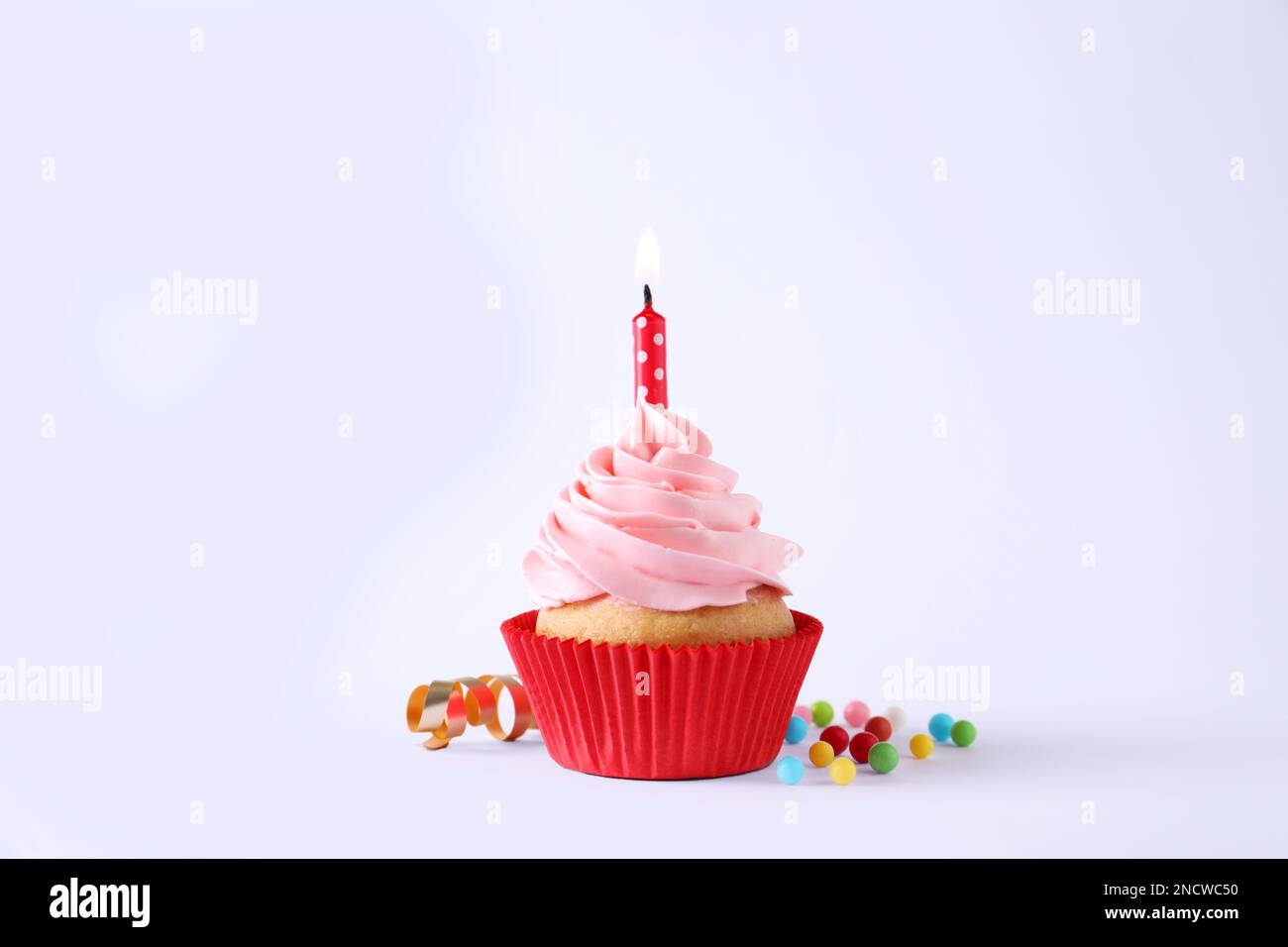 Delicious birthday cupcake with burning candle, sprinkles and streamer ...