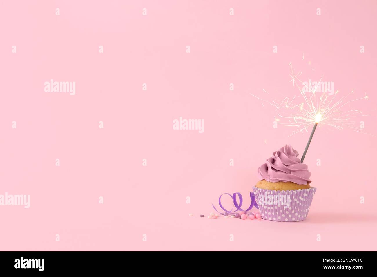 Birthday cupcake with burning sparkler, streamer and sprinkles on pink ...