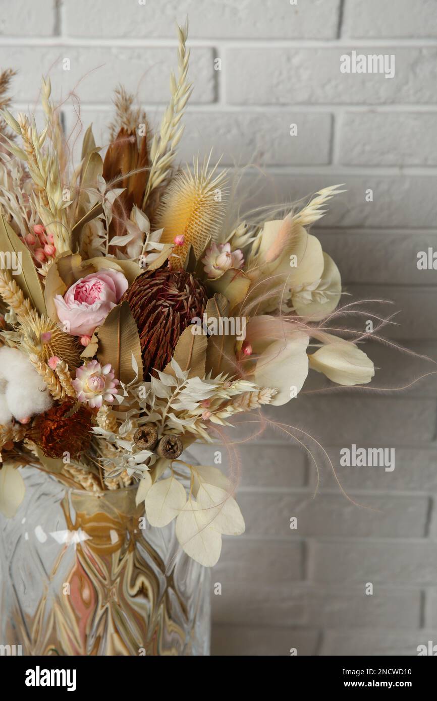 Beautiful dried flower bouquet in glass vase near white brick wall ...