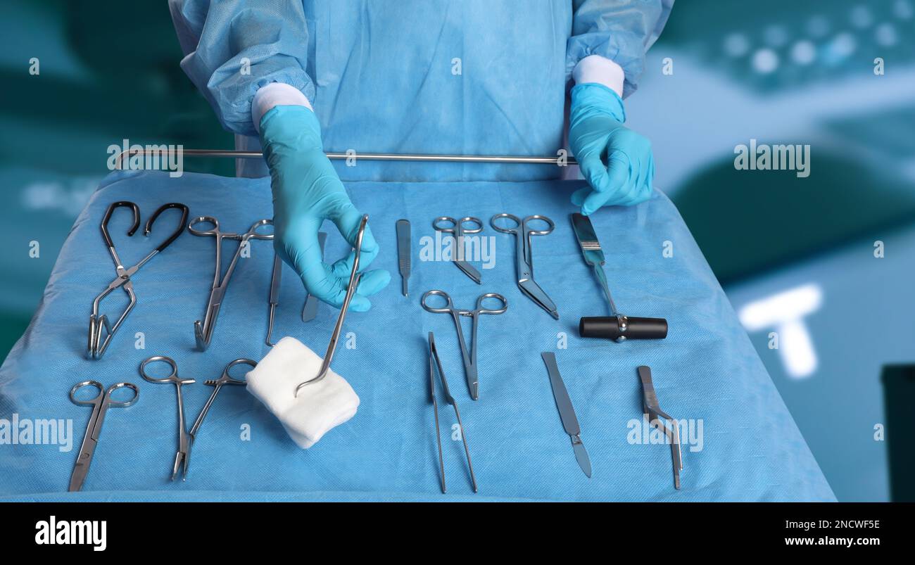 Nurse near table with different surgical instruments in operating room ...