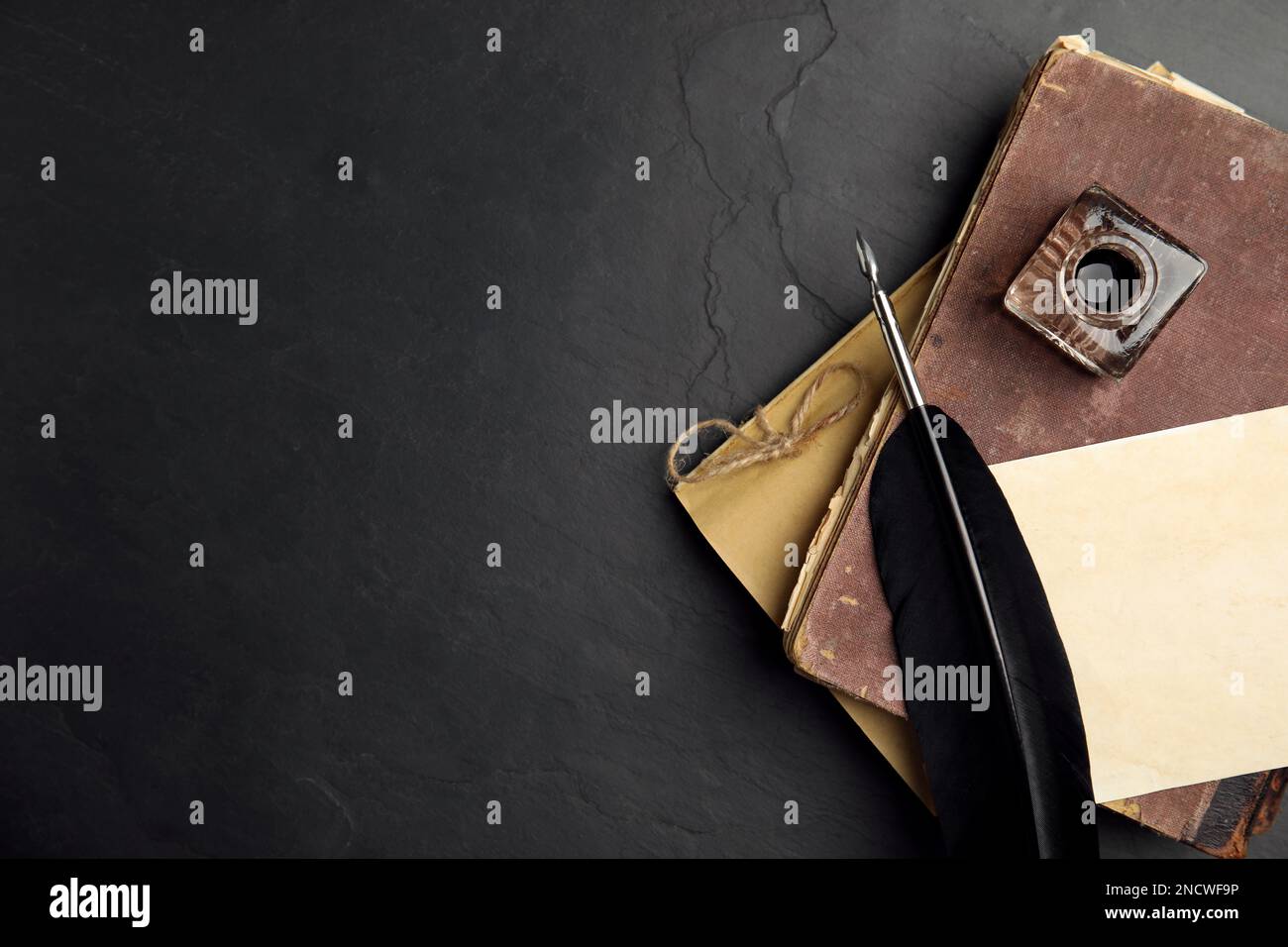 Feather pen, inkwell and old books on black table, top view. Space for ...