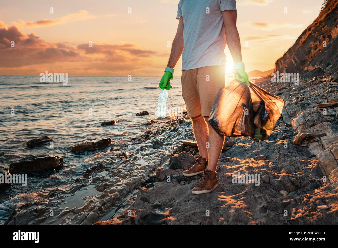 Close up of volunteer stand at the wild beach with a plastic bag and a ...