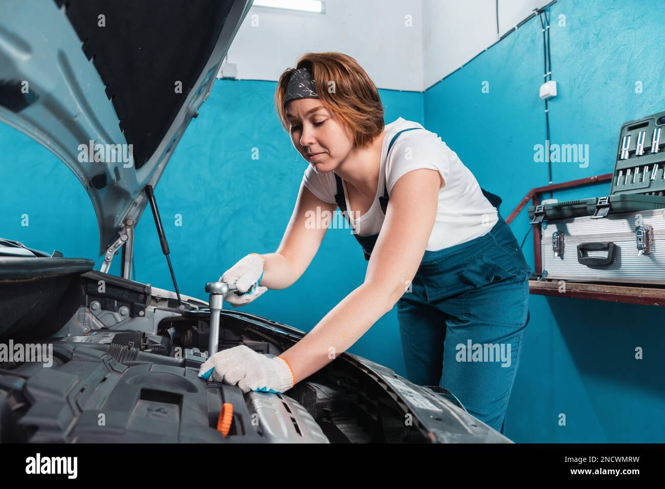 Mechanic woman in coveralls repair a engine with ratchet wrench. The ...