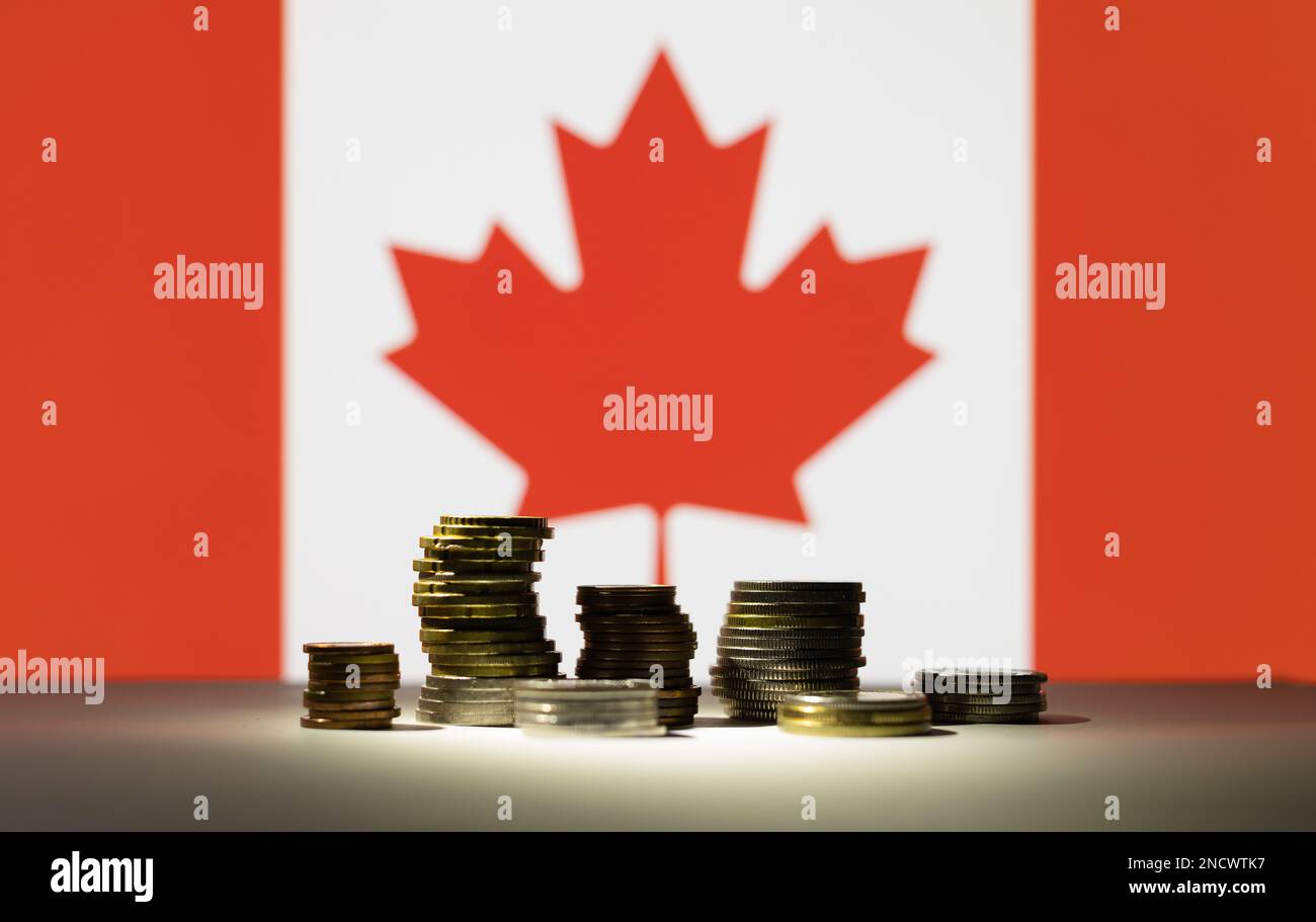 Stacked coins on a white table and a Canada flag in a background ...