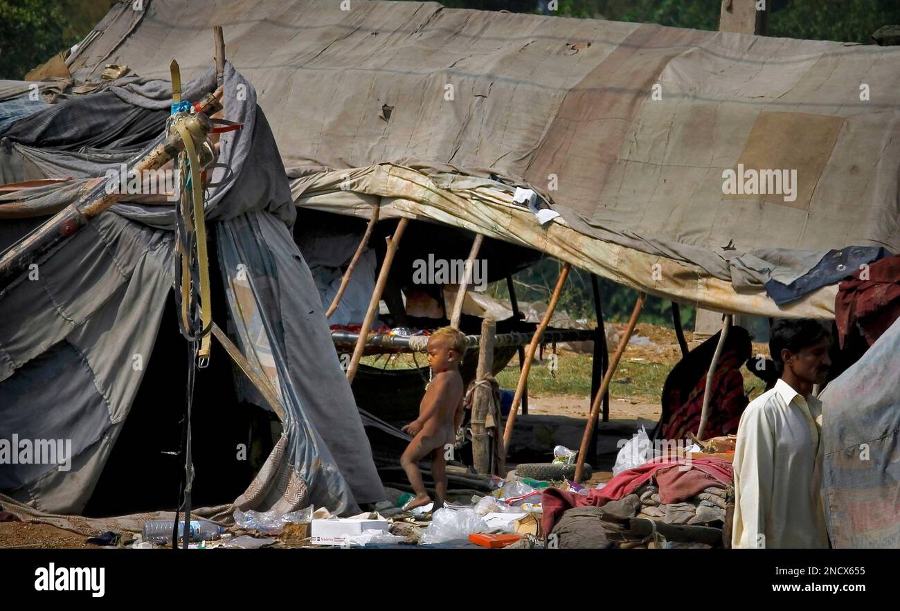 A poor child plays outside his makeshift tent set up along the roadside ...