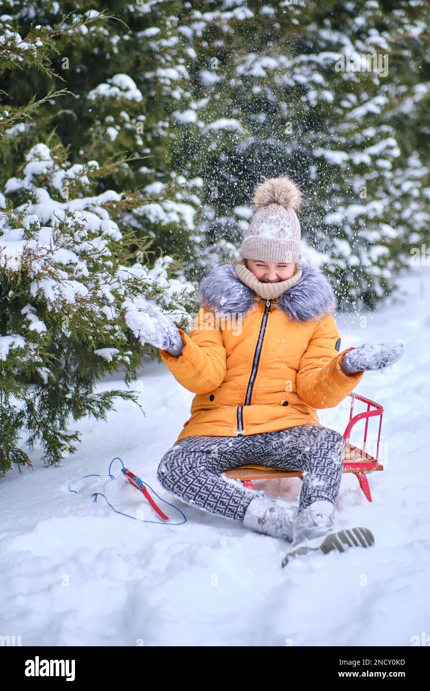 Kid girl enjoying snowy winter. Child sledding, sits on a sled and ...