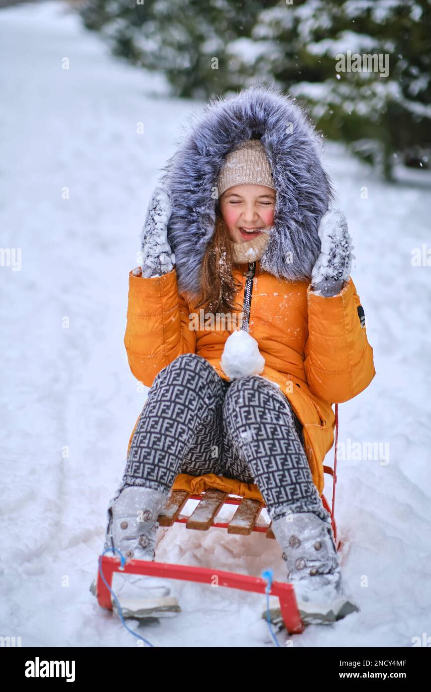 Kid girl enjoying snowy winter. Child sledding, sits on a sled and ...