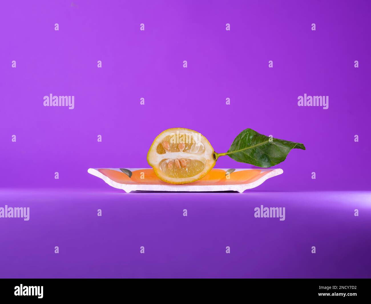 Cross-section of a lemon and a ceramic plate against a purple ...