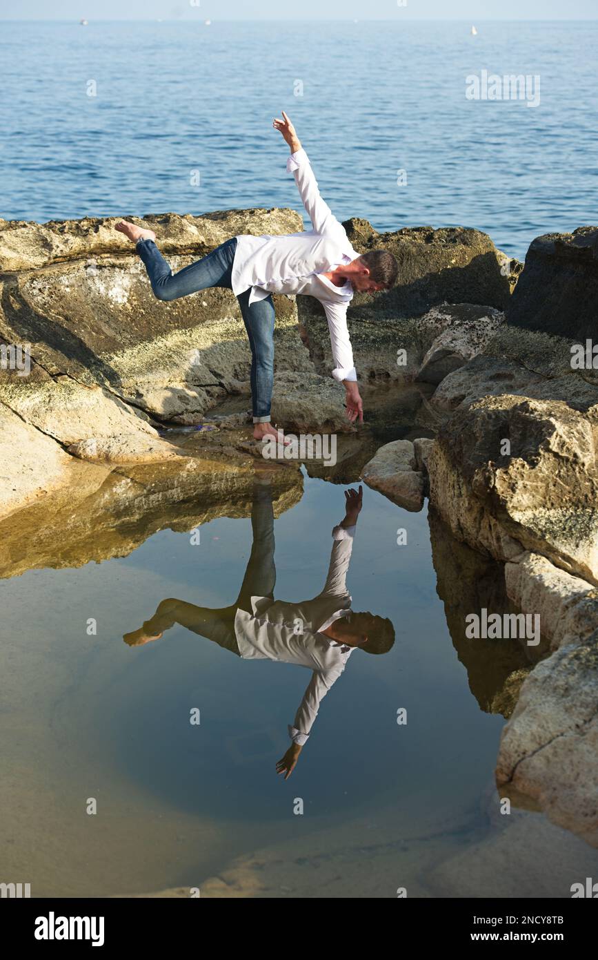 Young man standing on one leg at the edge of a rock pool, Valletta ...